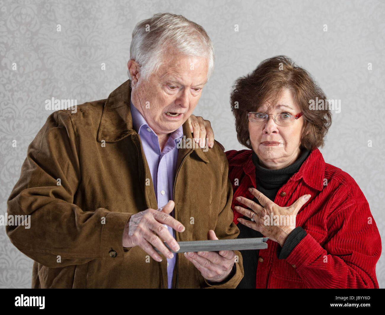 Angry man using tablet with embarrassed woman Stock Photo - Alamy
