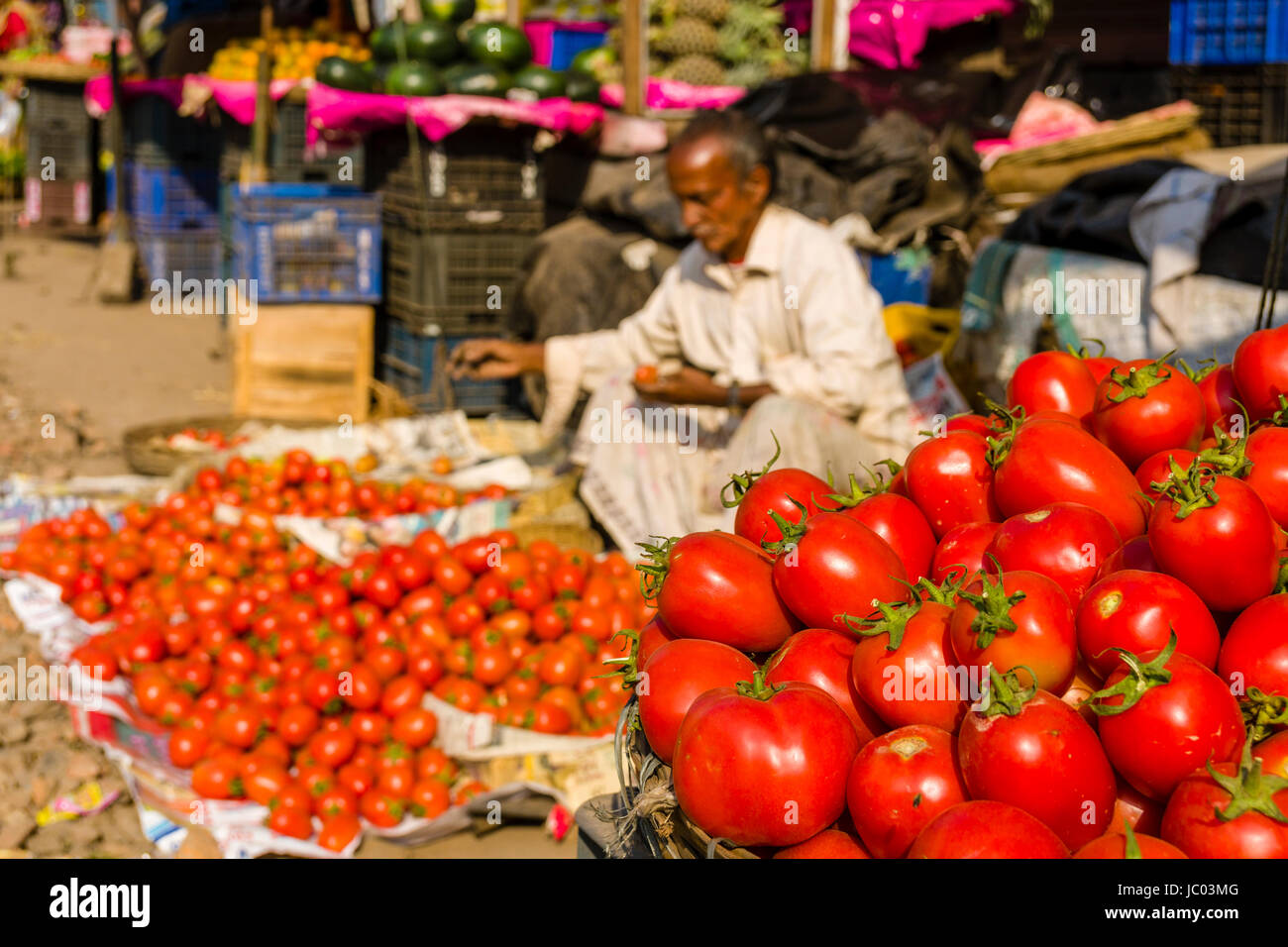 A man is selling tomatoes on a busy vegetable market street in the ...