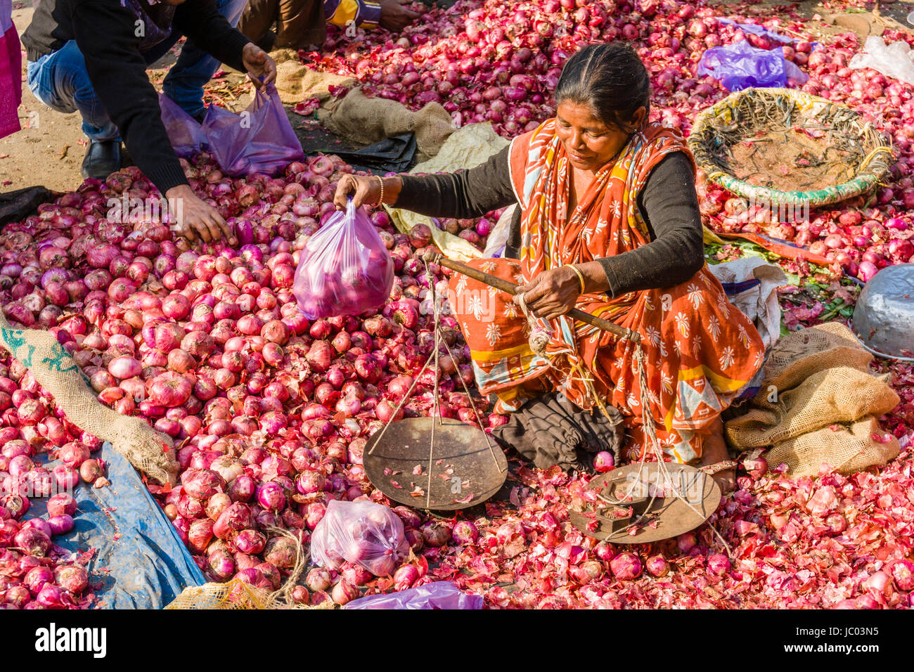 A woman is selling onions on a busy vegetable market street in the ...