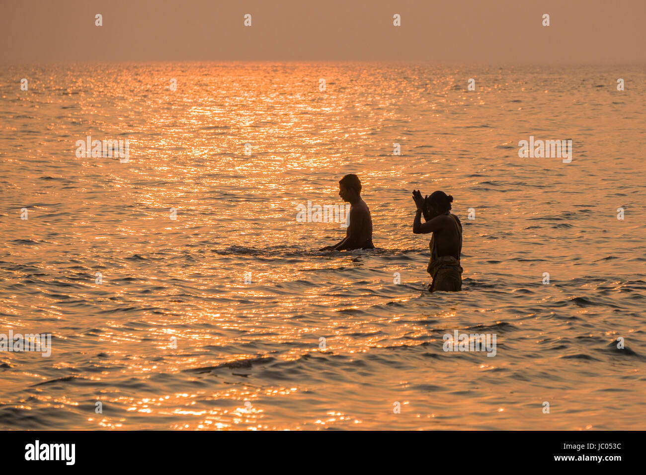 Two pilgrims are praying in the water at Ganga Sagar at sunset ...
