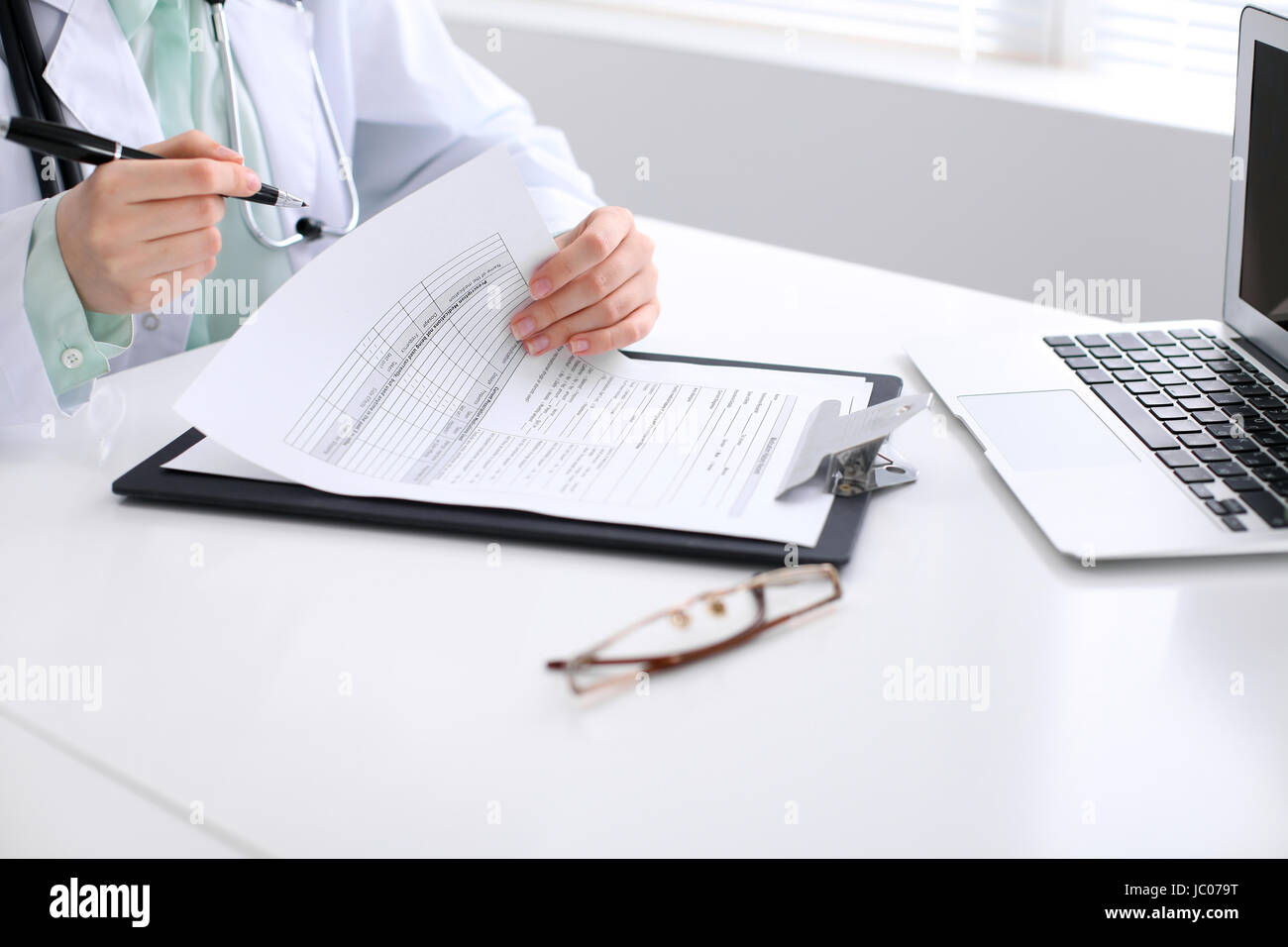 Close-up of a female doctor filling out application form , sitting at ...