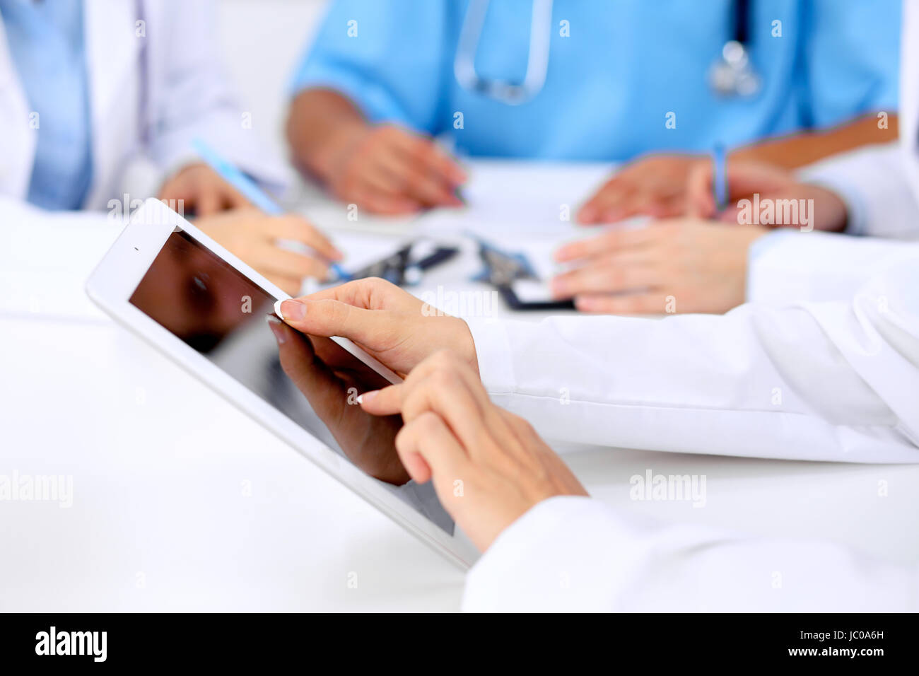 Group of doctors at medical meeting. Close up of physician using tablet ...