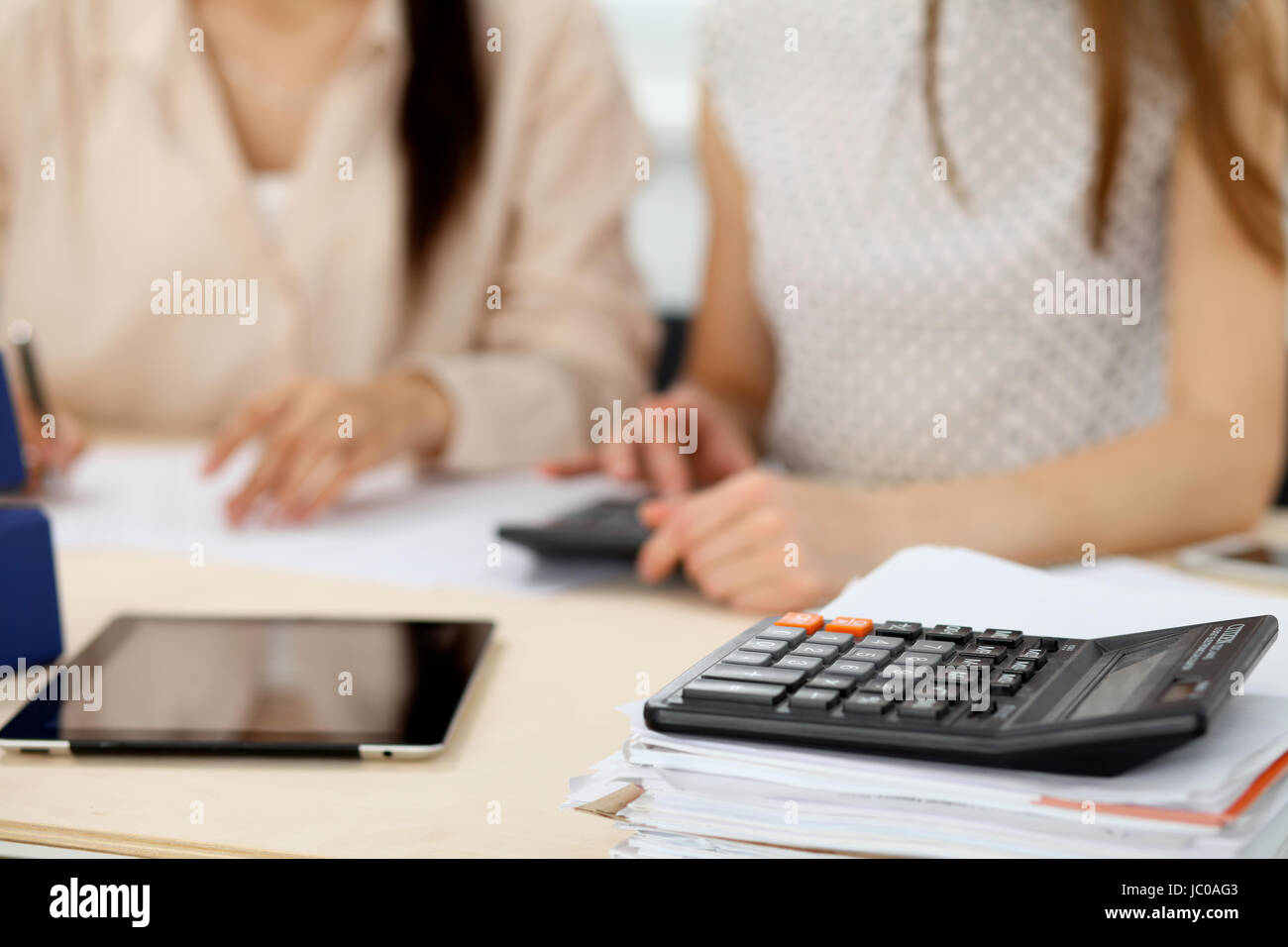Two female accountants counting on calculator income for tax form ...