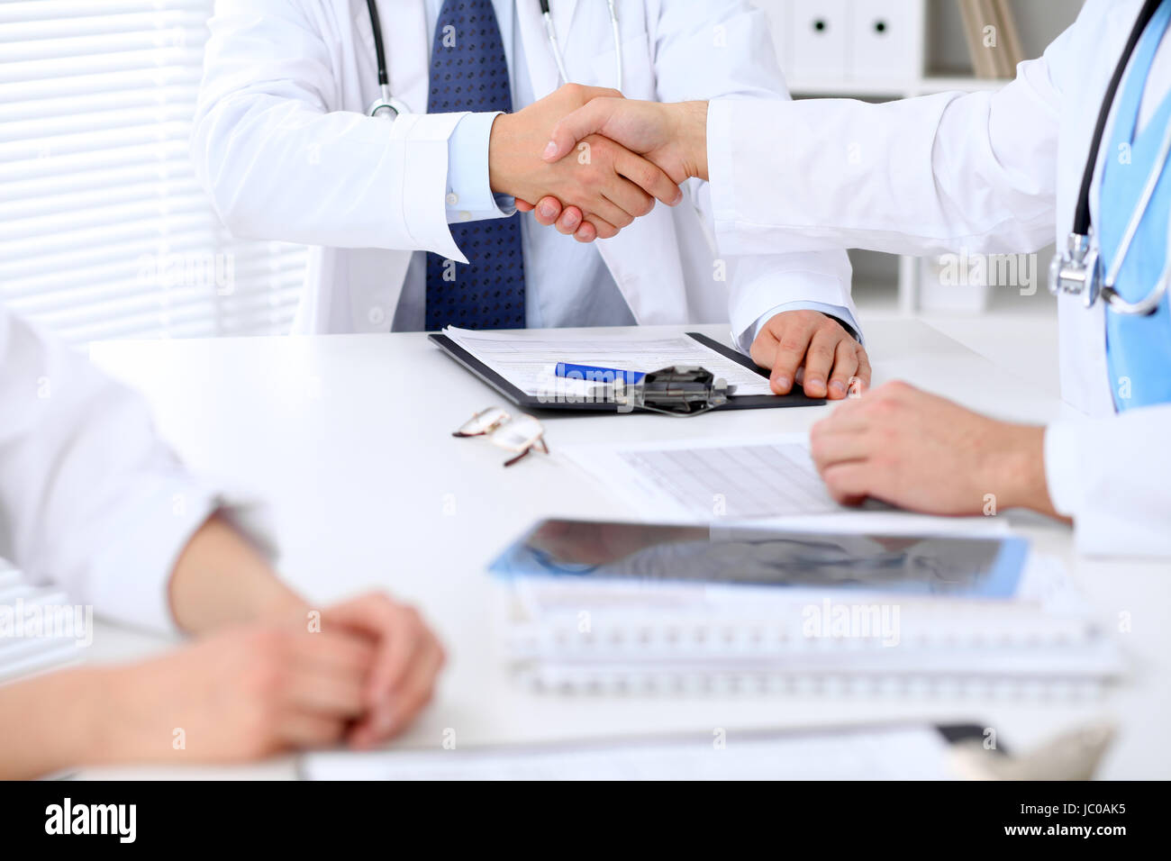 Two doctors shaking hands to each other sitting at the table in ...
