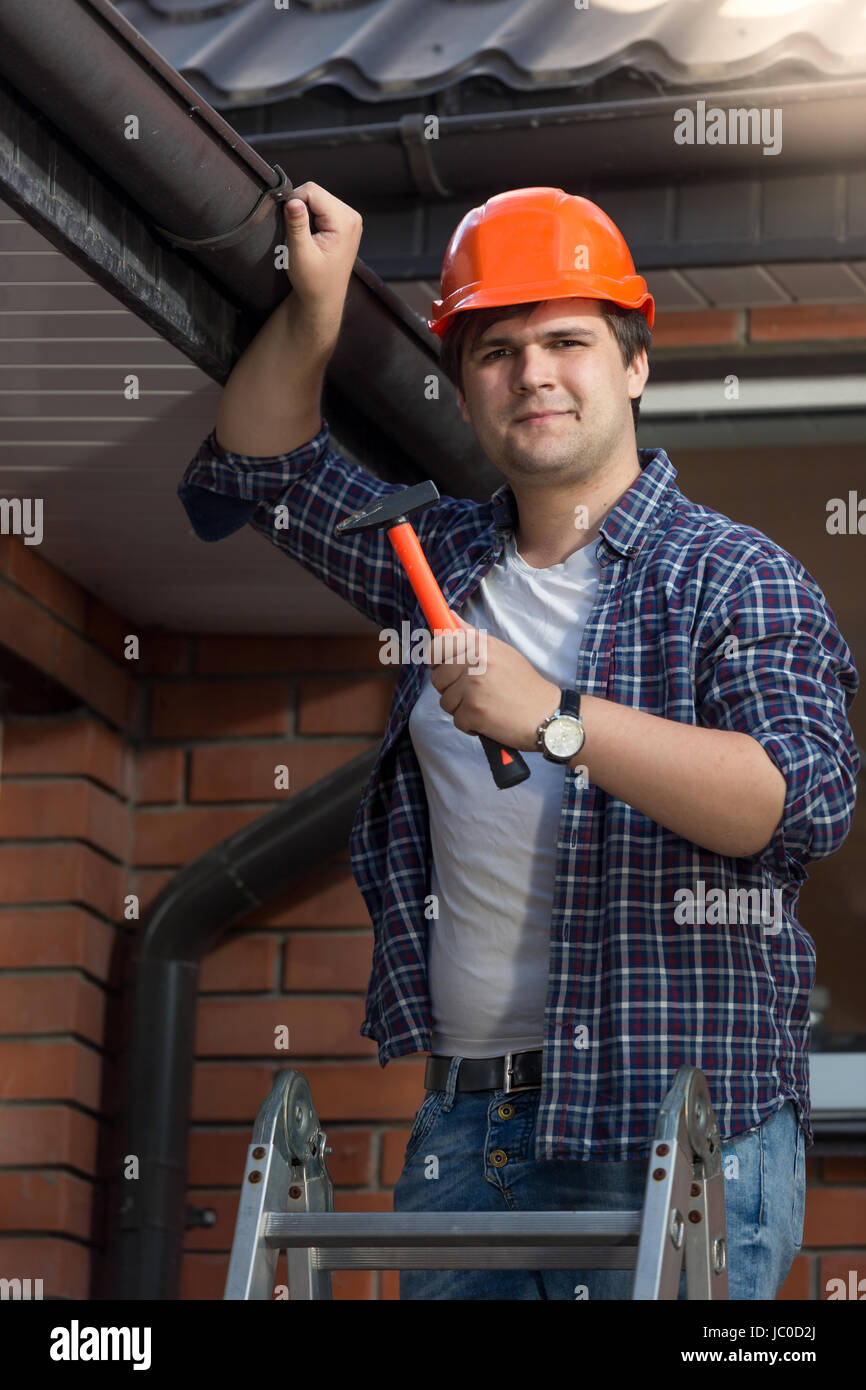 Portrait of handsome worker in hardhat posing with hammer on step ...