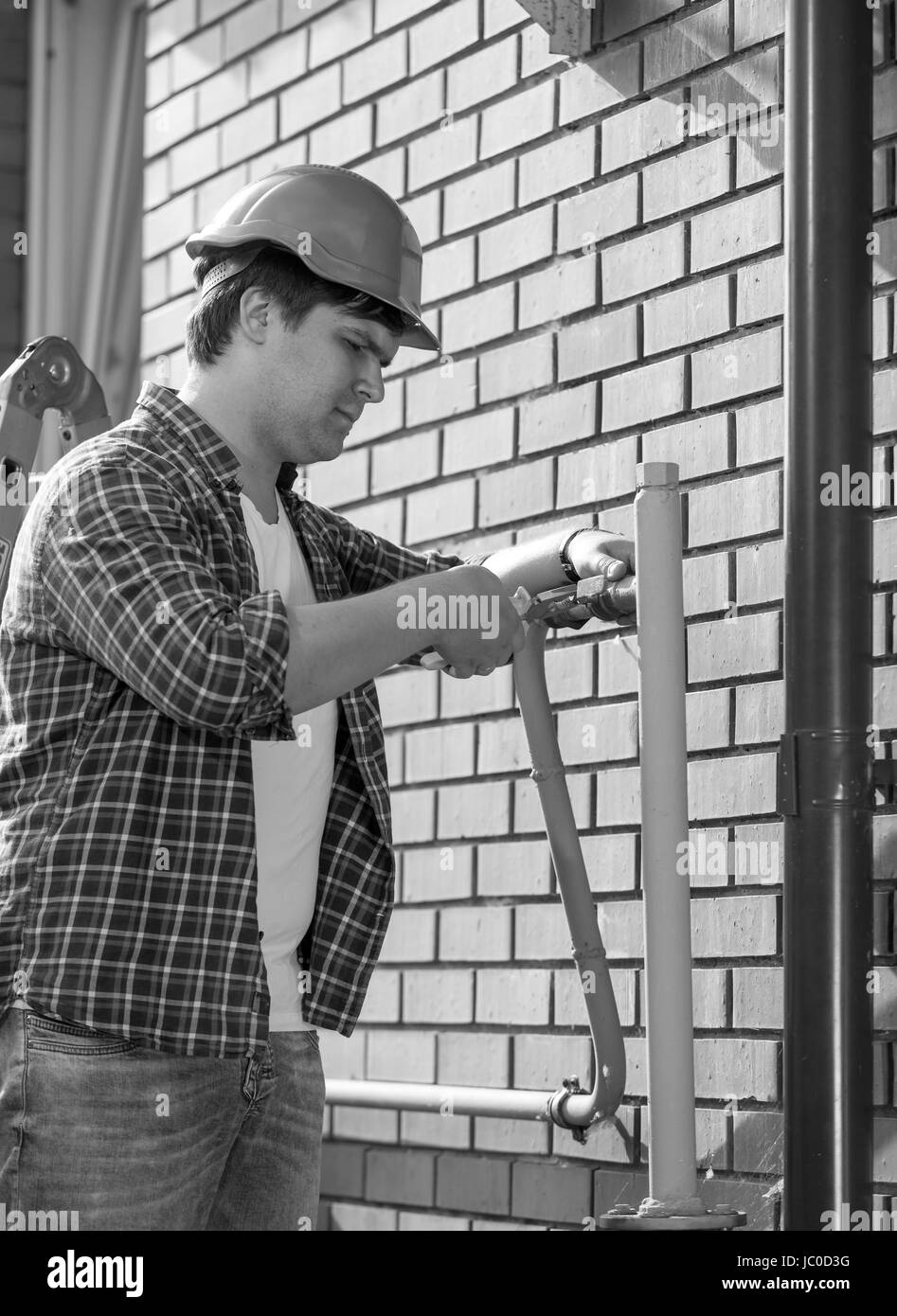 Black and white portrait of plumber assembling pipes on house outer ...