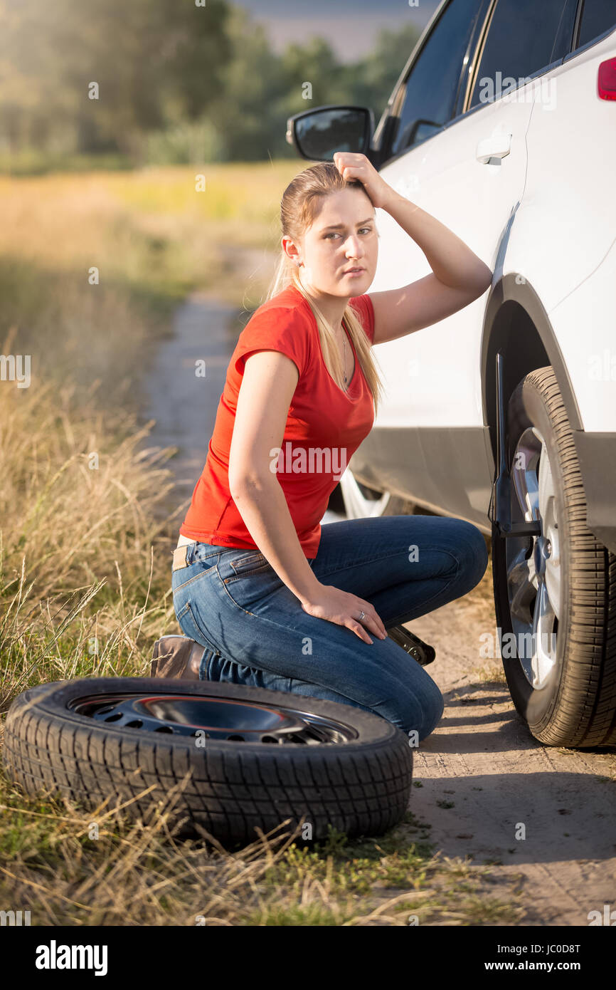 Sad woman sitting at broken car and trying to change flat tire Stock ...