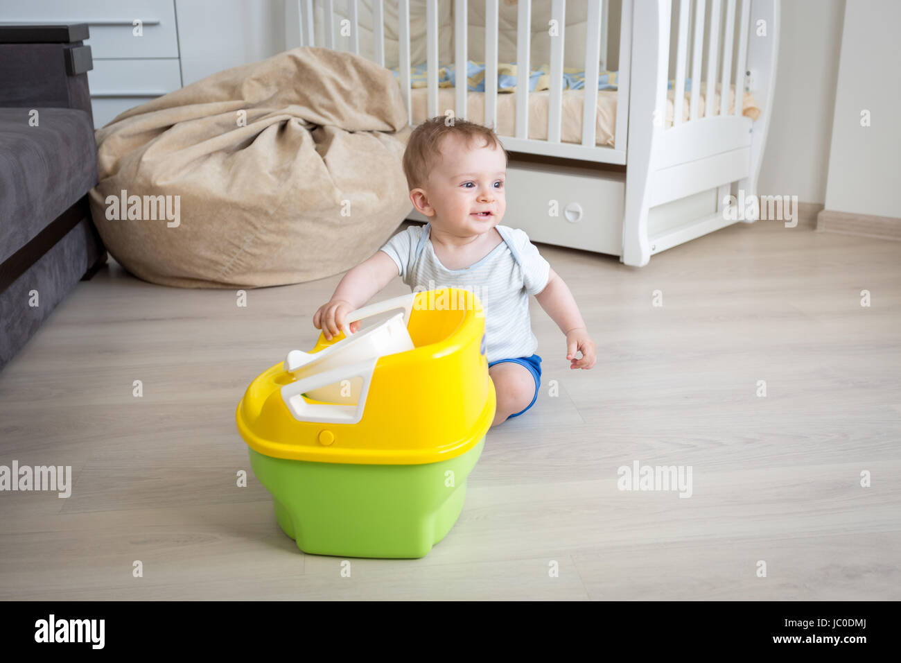 Adorable baby boy playing with chamber pot on floor at living room ...
