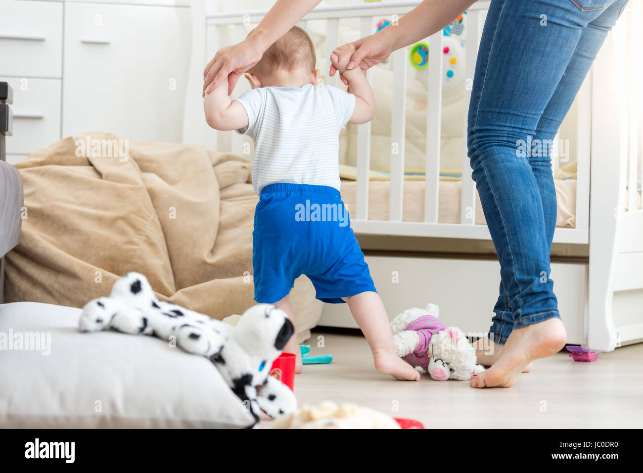 Adorable baby boy making first steps with mother at living room Stock ...