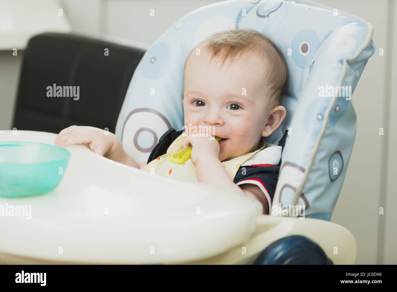 Toned portrait of smiling baby boy sitting in highchair and eating ...