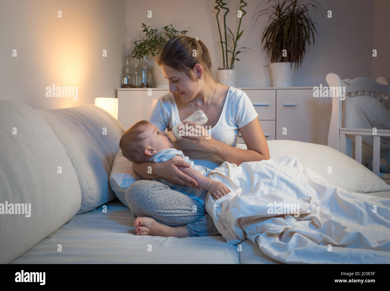 Portrait of beautiful young woman giving milk from bottle to her baby ...