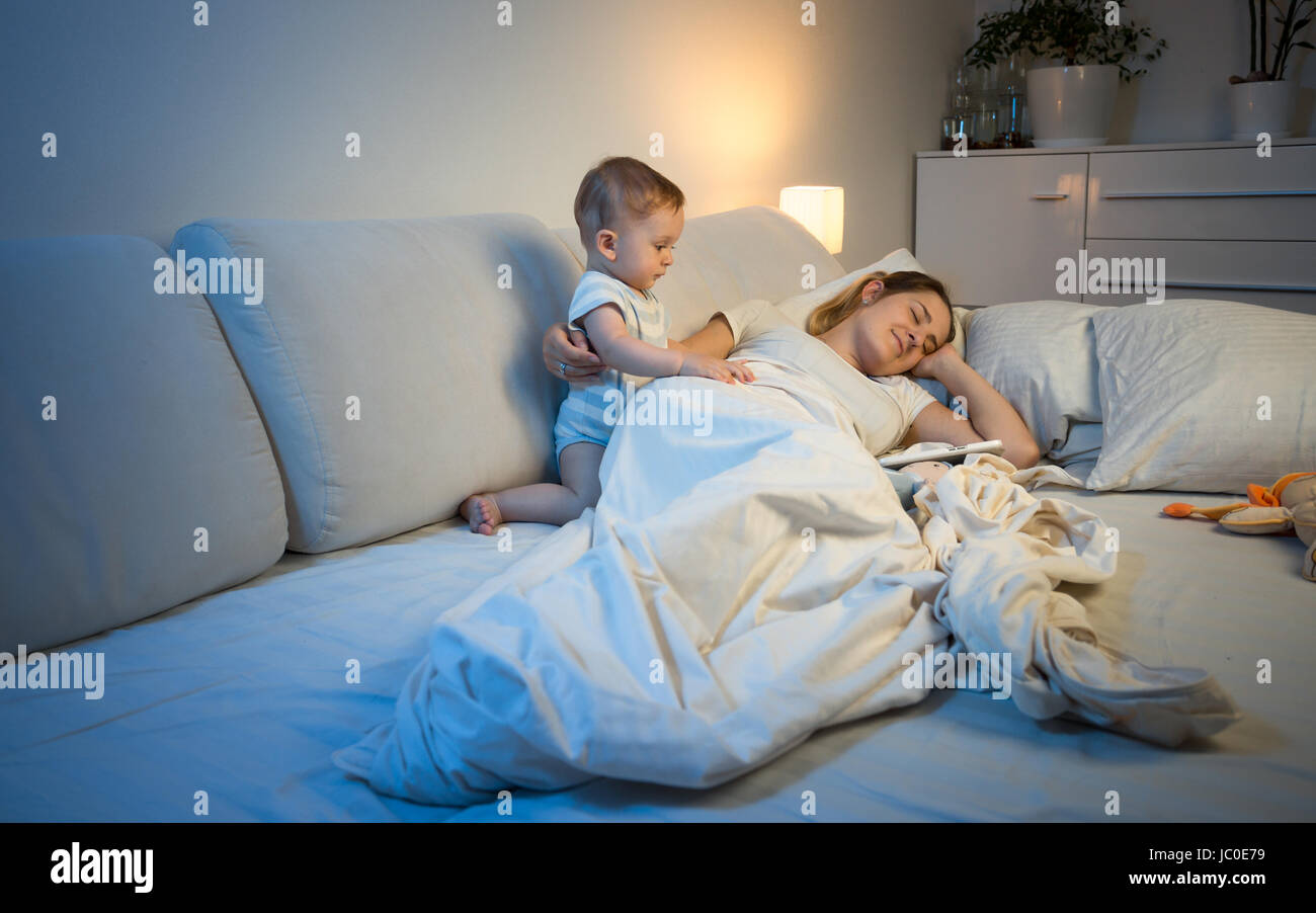 Cute sleepless baby boy waking up his mother sleeping in bed Stock ...