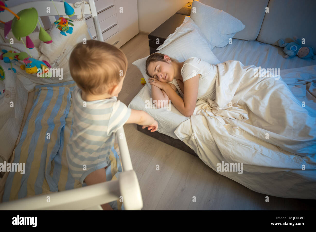 Baby in cot crying and trying to wake up mother that fell asleep Stock ...