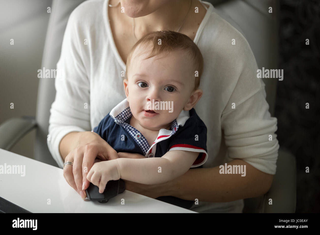 Portrait of cute baby boy sitting on mothers lap while she is working ...