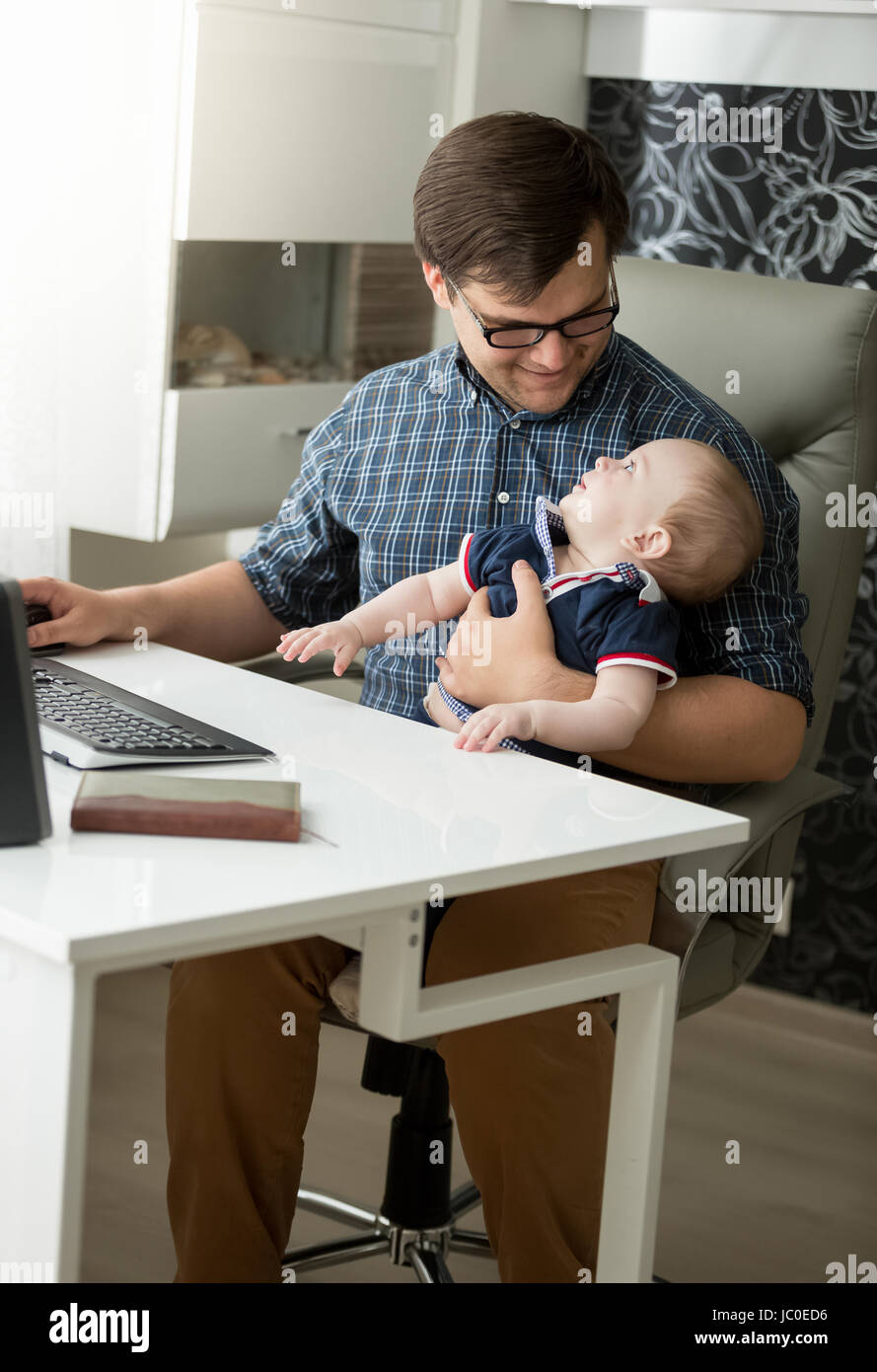 Portrait of young man sitting with his baby and working at home Stock ...