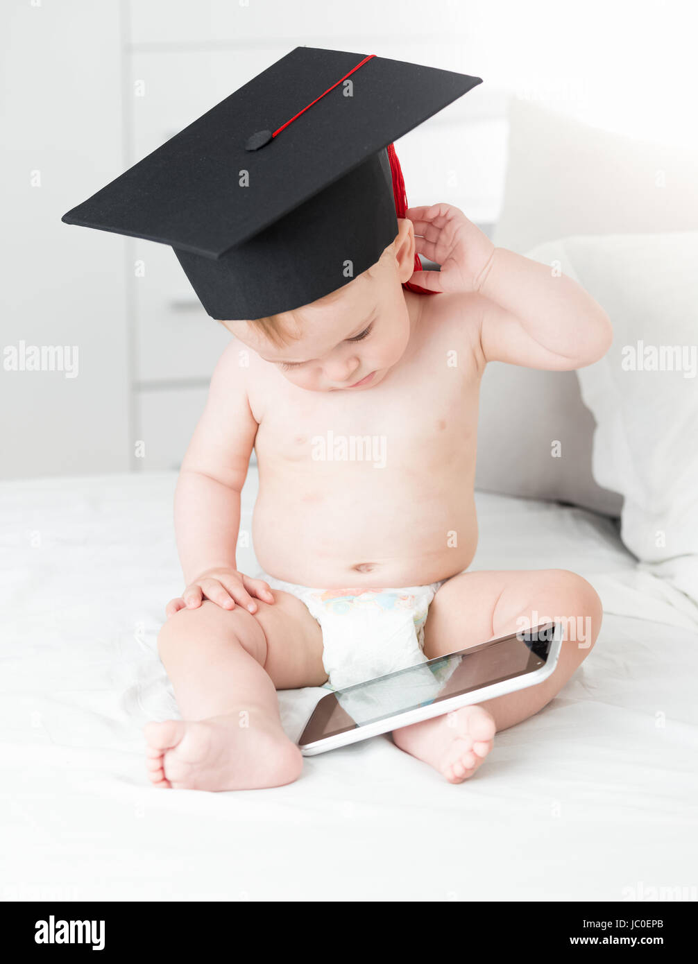 Adorable baby boy wearing graduation cap and using digital tablet ...