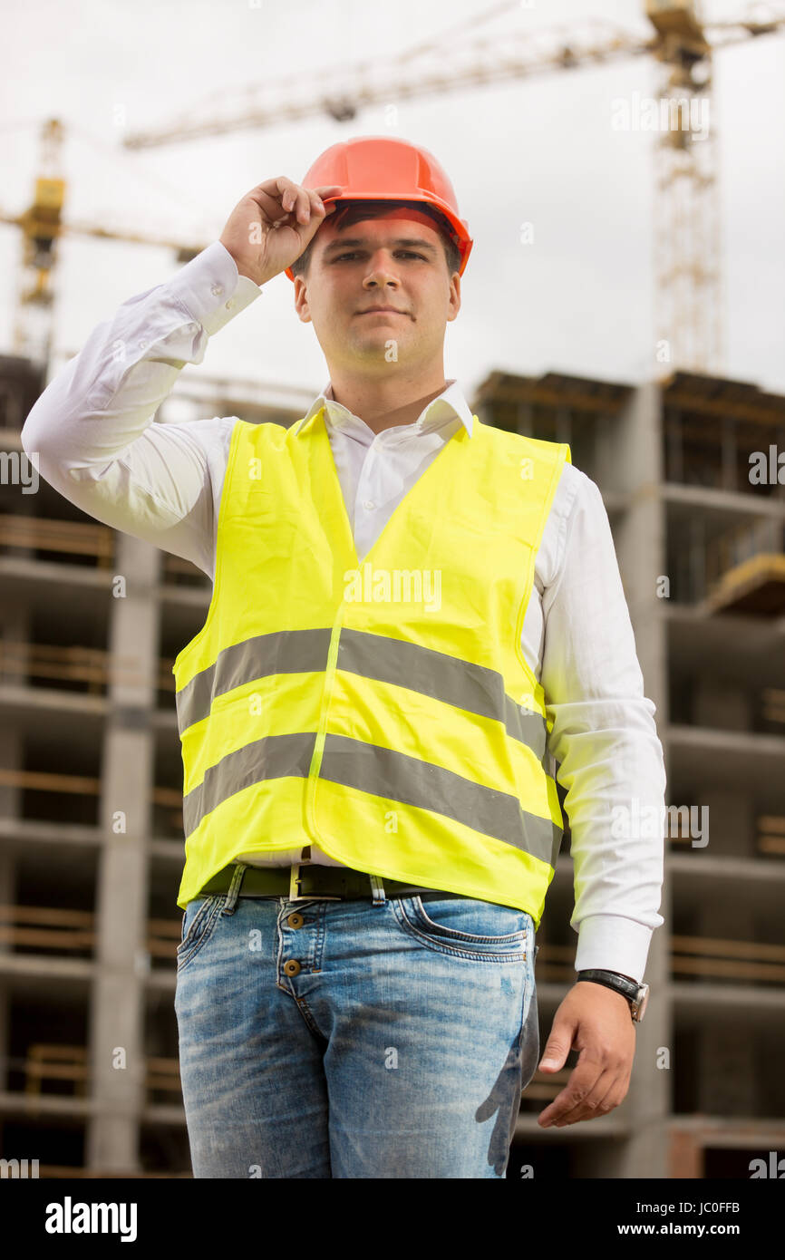 Portrait of handsome smiling engineer in hardhat posing against working ...