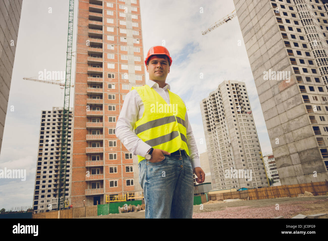 Toned portrait of smiling engineer posing against buildings under ...