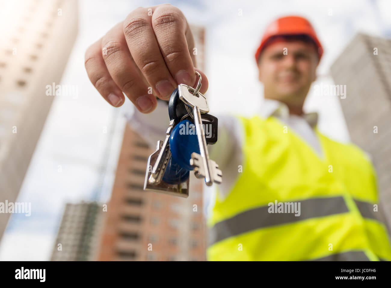 Portrait of young smiling construction engineer holding keys from new ...