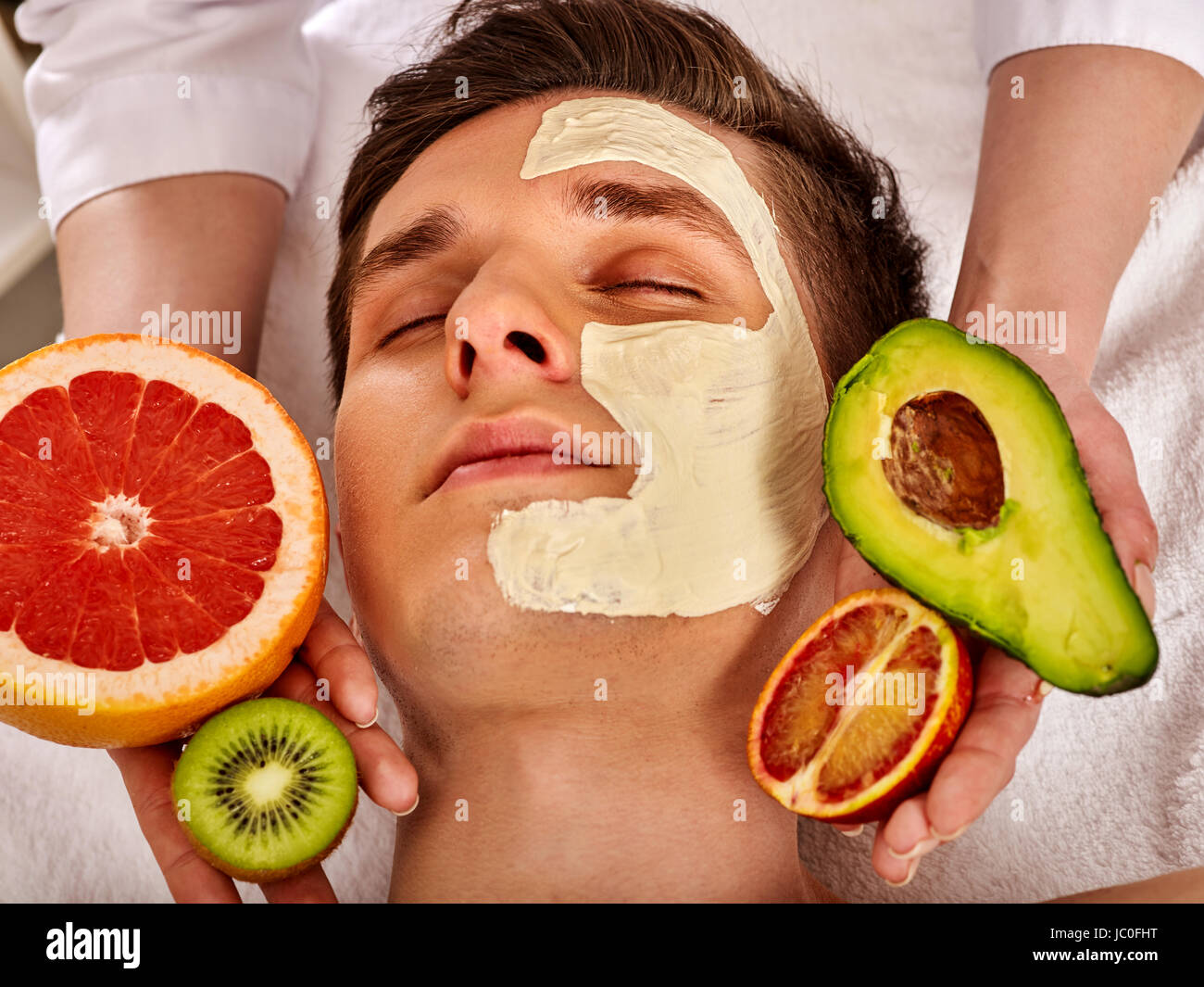 Facial mask from fresh fruits and clay for man. Beautician apply slices ...
