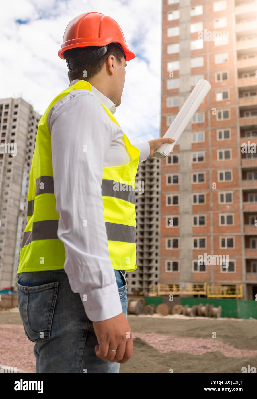 Portrait of building inspector pointing at building under construction ...
