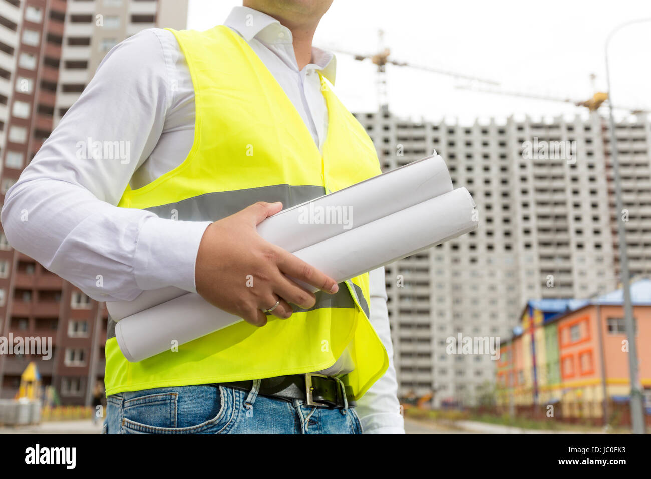 Closeup photo of engineer holding rolled blueprints in background of ...