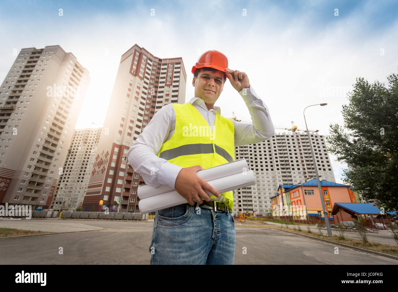 Portrait of young engineer standing at new buildings with blueprints ...