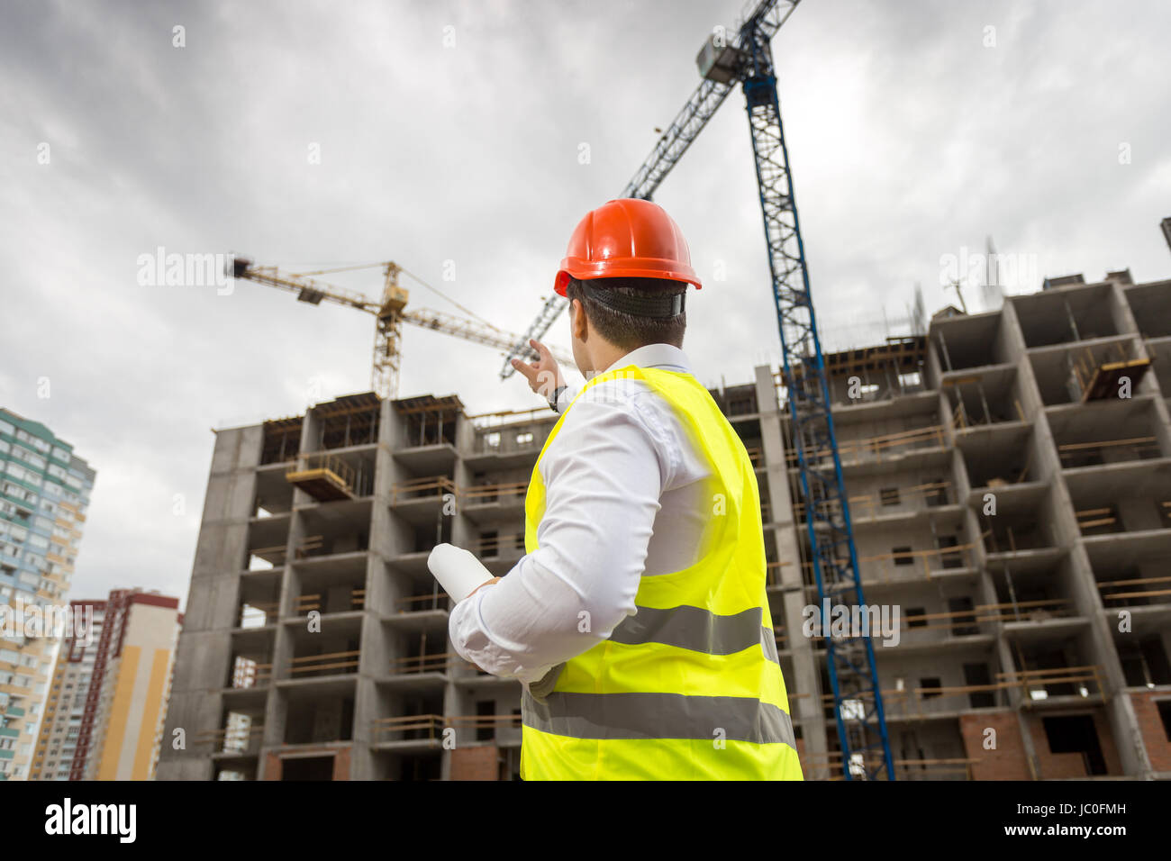 Rear view of architect in hardhat pointing at building under ...