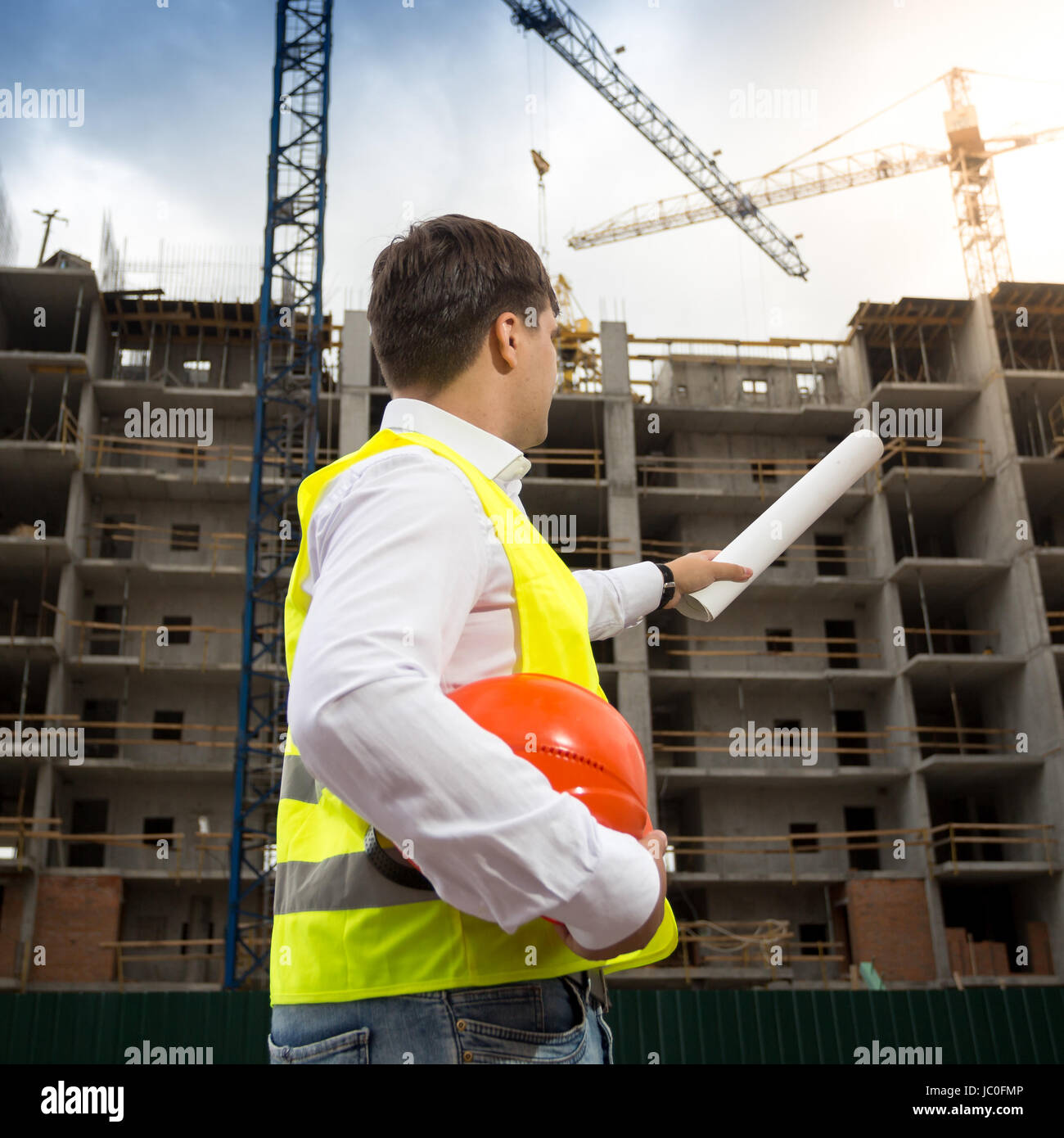 Rear view image of young engineer pointing at building with rolled ...