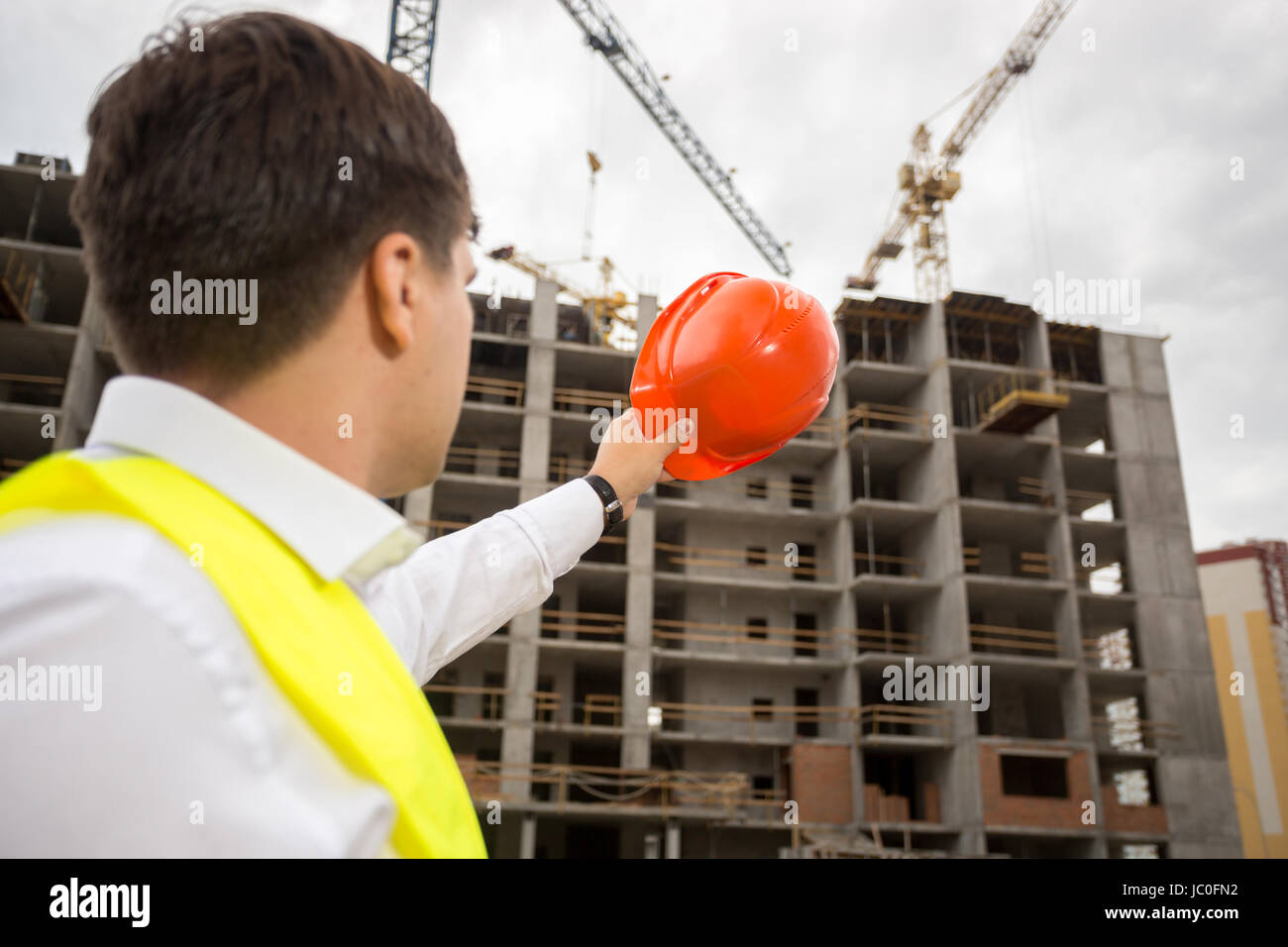 Portrait of young construction engineer pointing at building under ...
