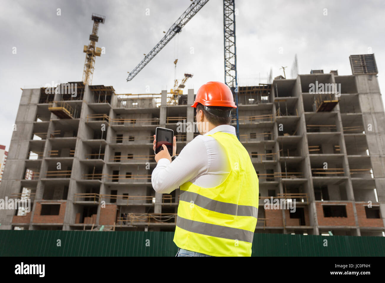 Rear view of building inspector holding digital tablet and inspecting ...