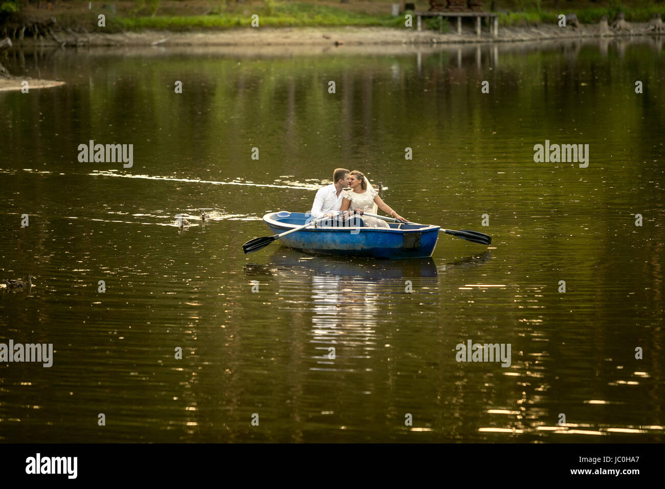 Beautiful newly married couple kissing on rowing boat in the middle of ...