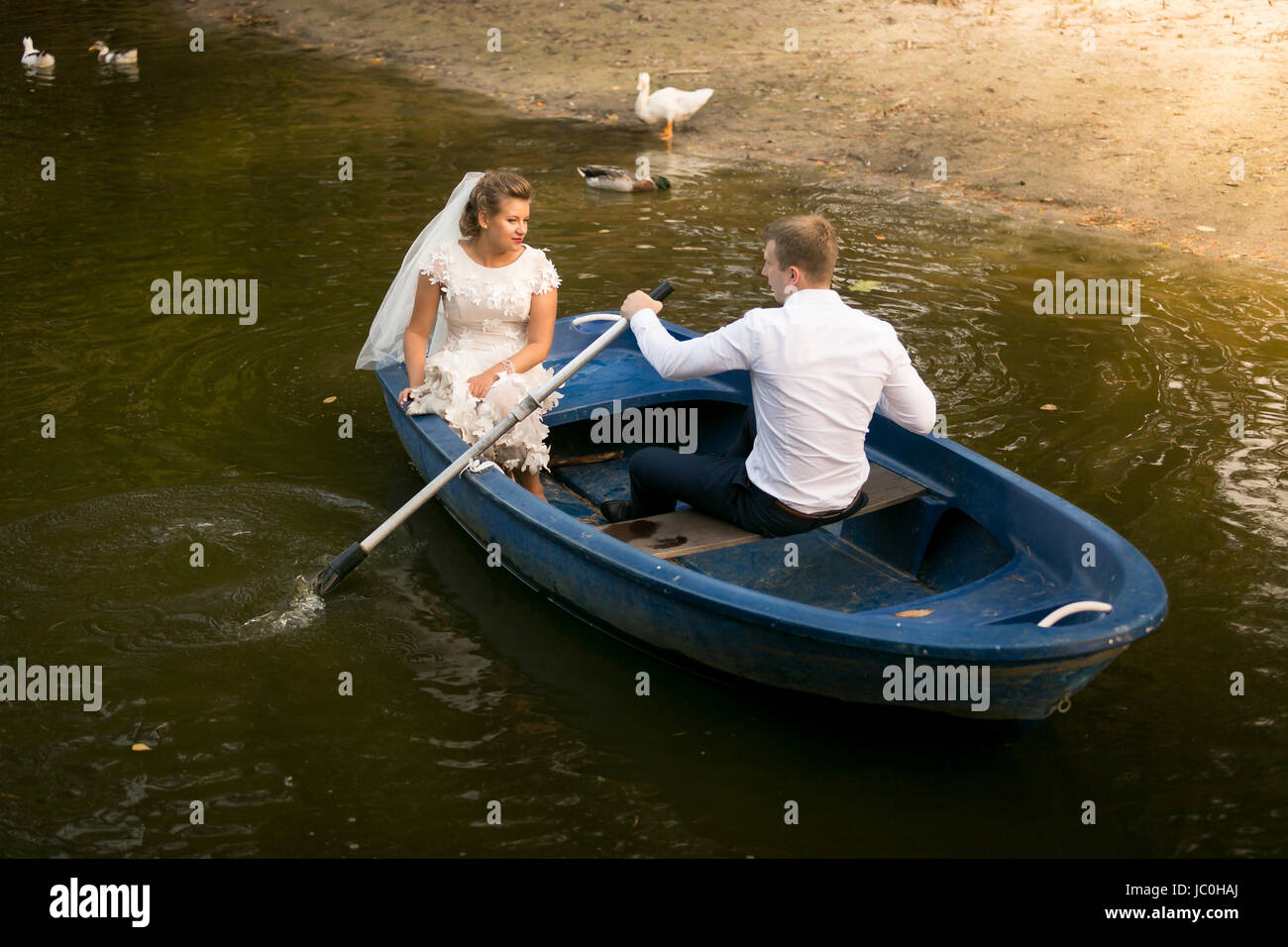 Happy newly married couple riding on rowing boat on lake Stock Photo ...