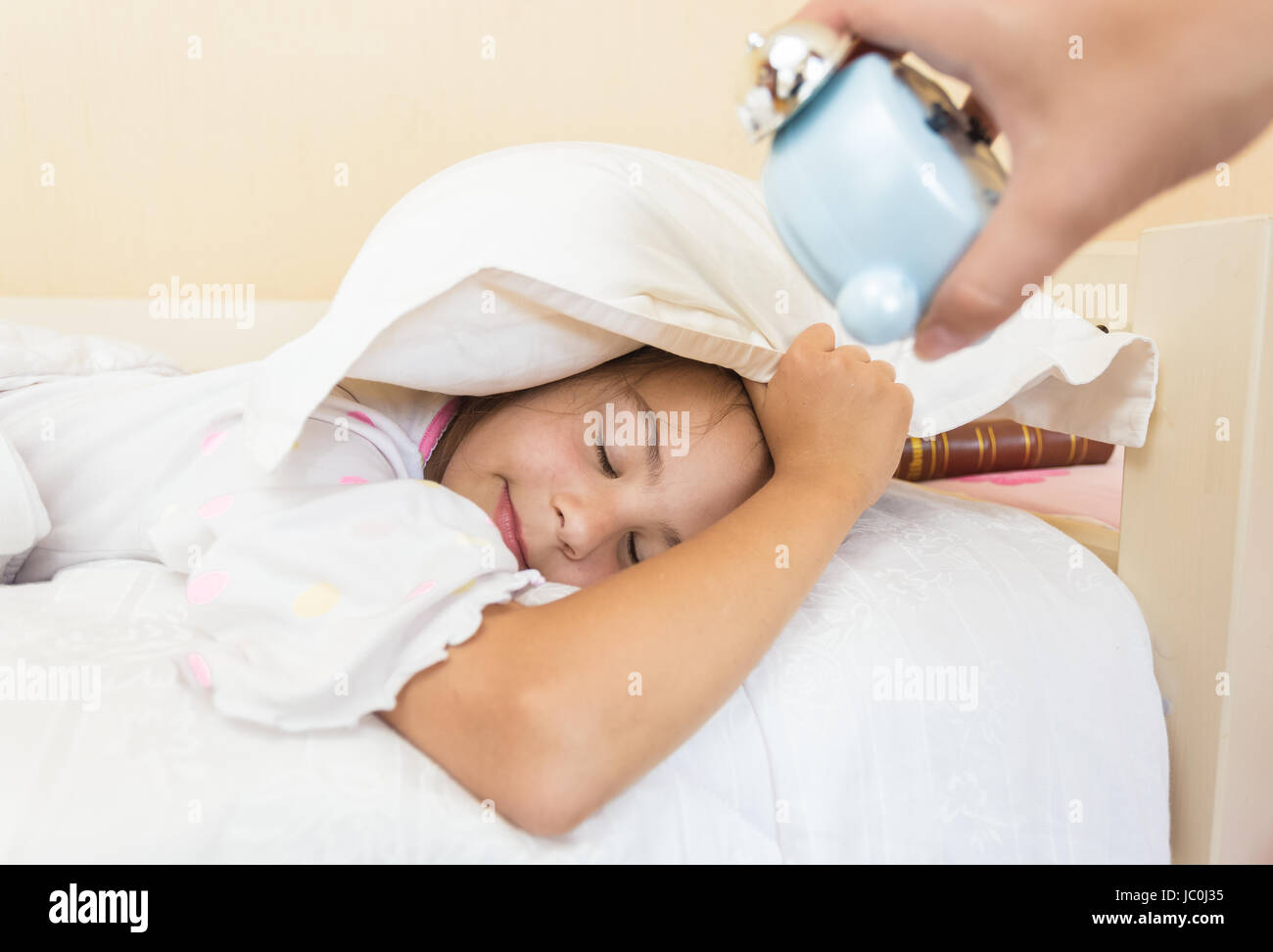 Closeup photo of mother holding alarm clock on sleeping daughters ear ...