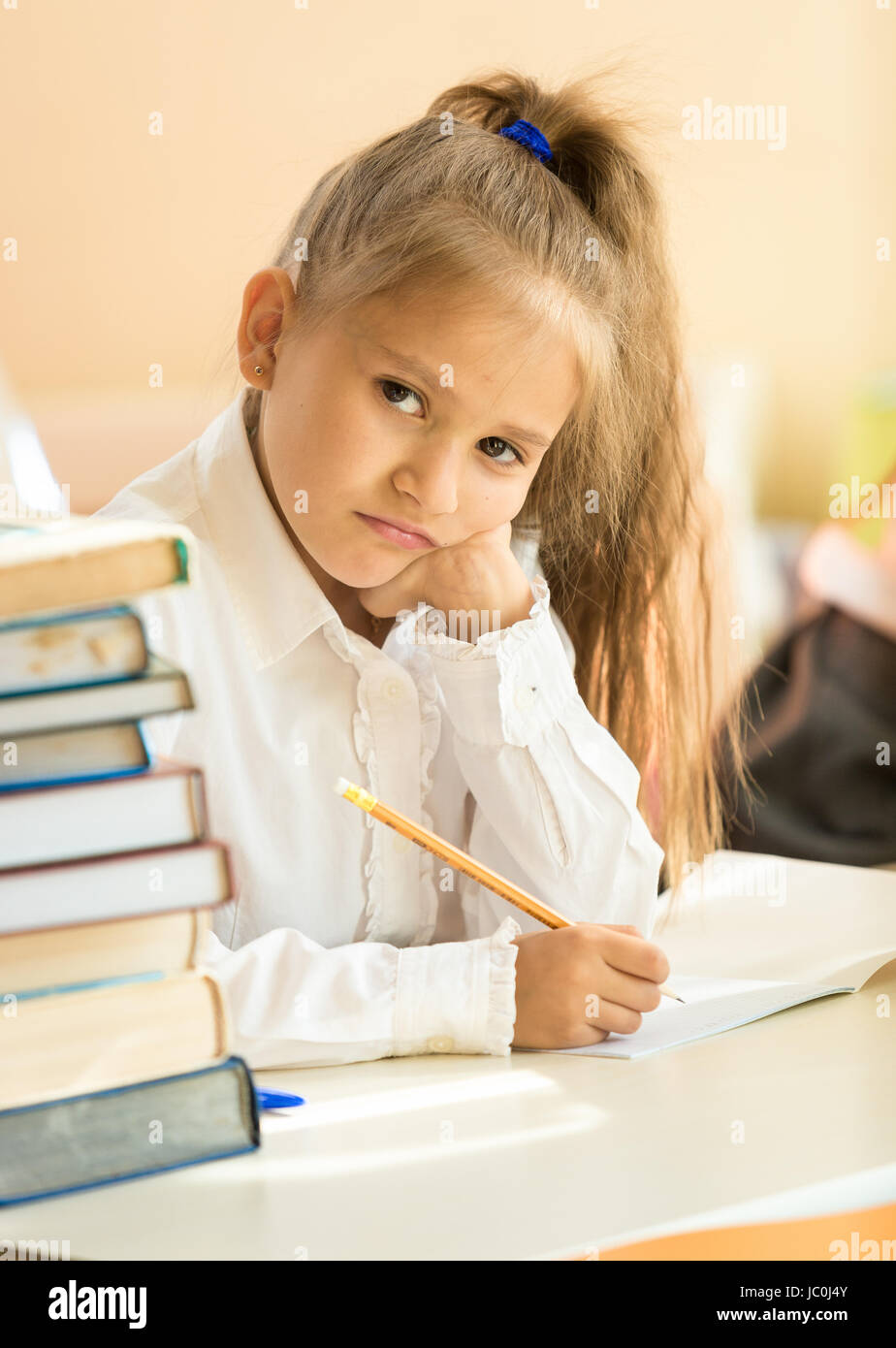 Portrait of upset girl writing test in classroom and looking at camera ...