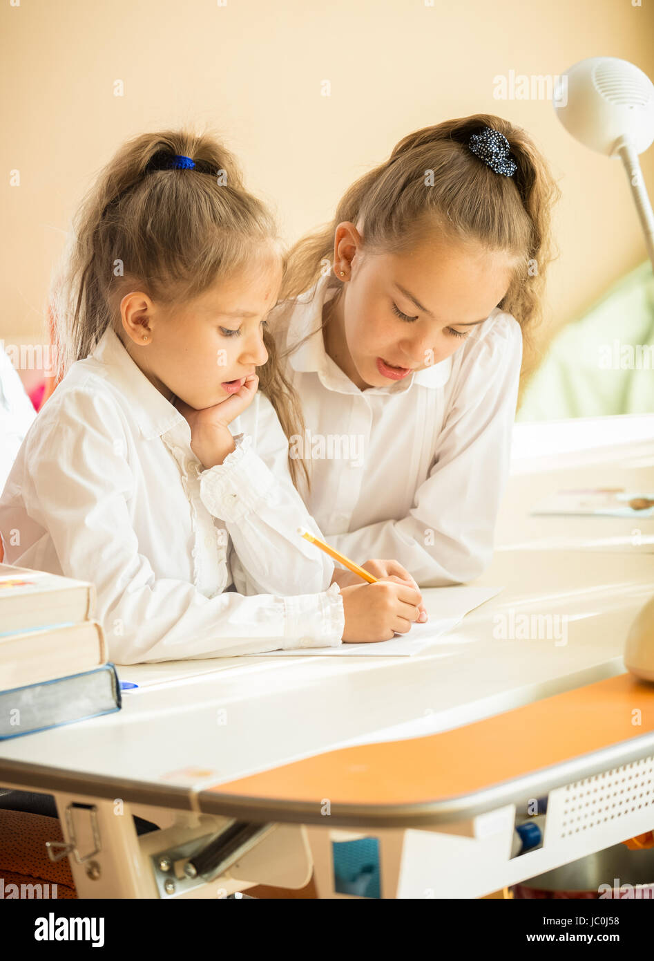 Portrait of two cute schoolgirls writing at textbook at desk Stock ...