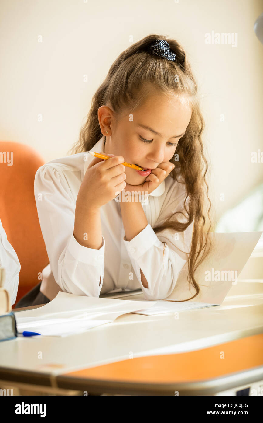 Closeup portrait of schoolgirl chewing pencil while doing homework ...