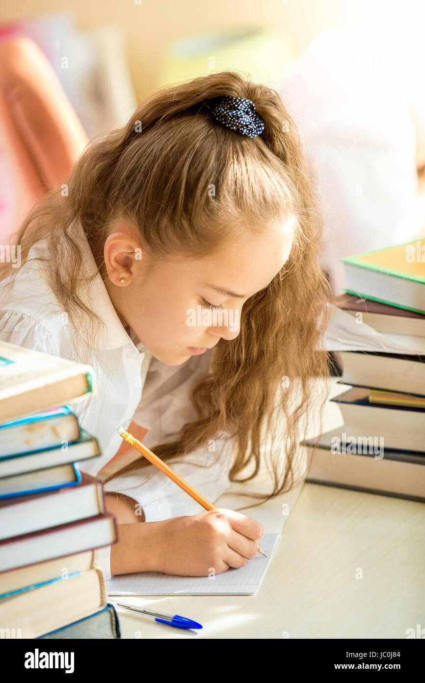 Portrait of brunette schoolgirl surrounded by books doing homework ...