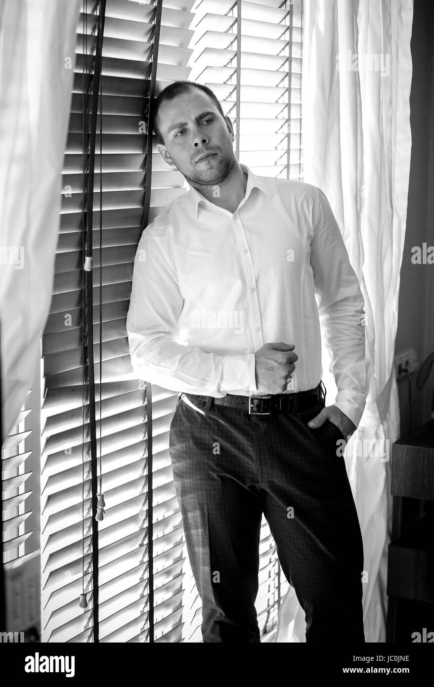 Black and white portrait of elegant businessman leaning against window ...