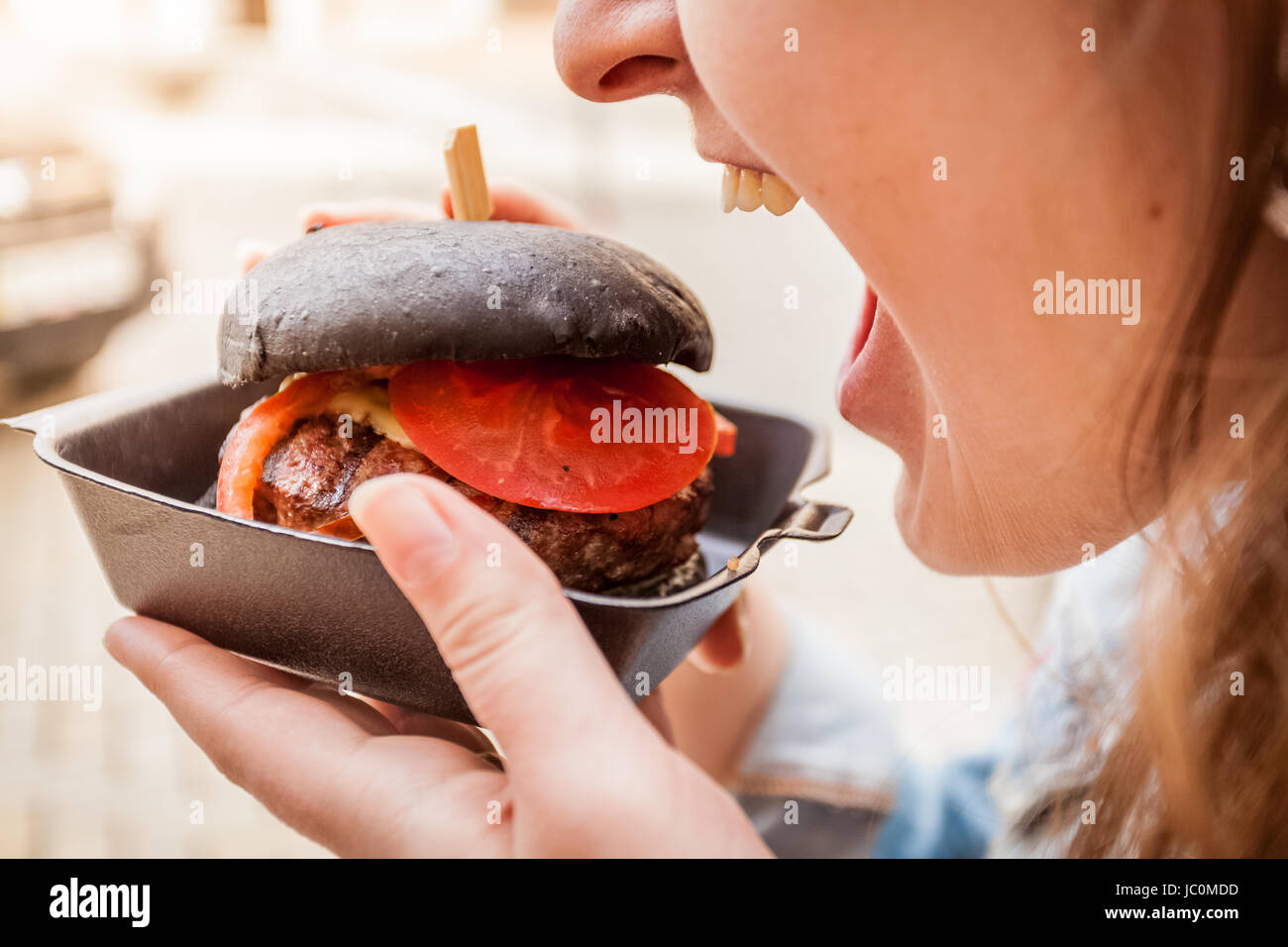 Portrait of woman biting black burger with marbled beef Stock Photo - Alamy