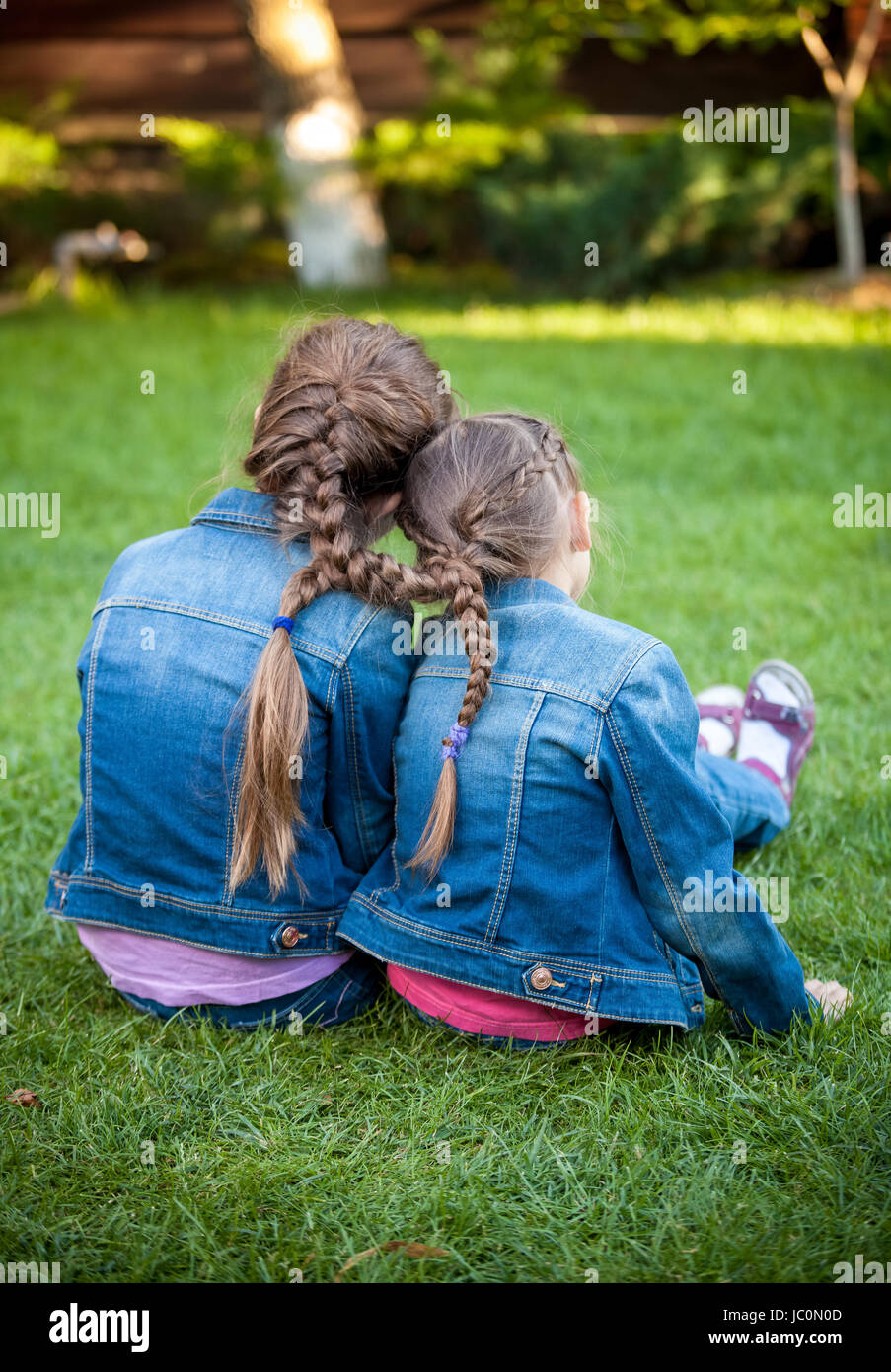 Two little sisters sitting on grass head to head with joint braids ...