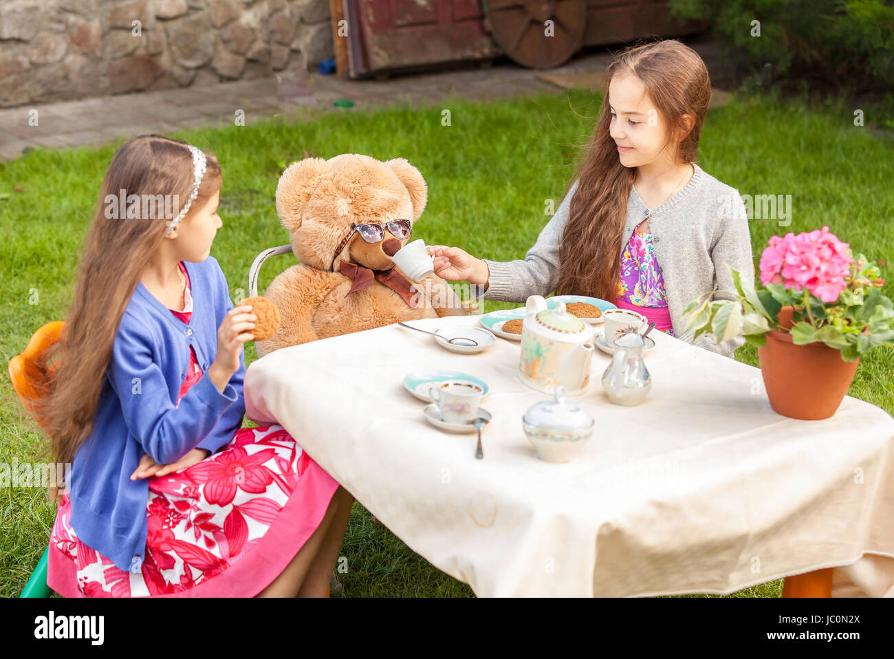 Two girls having tea party with teddy bear at yard Stock Photo - Alamy