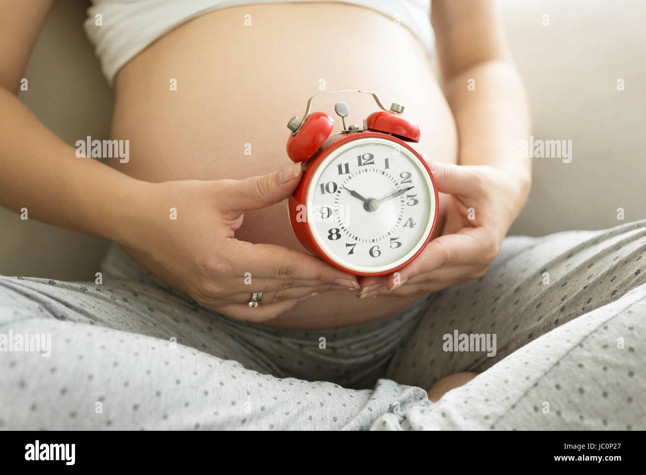 Closeup photo of pregnant woman holding red alarm clock at tummy Stock ...