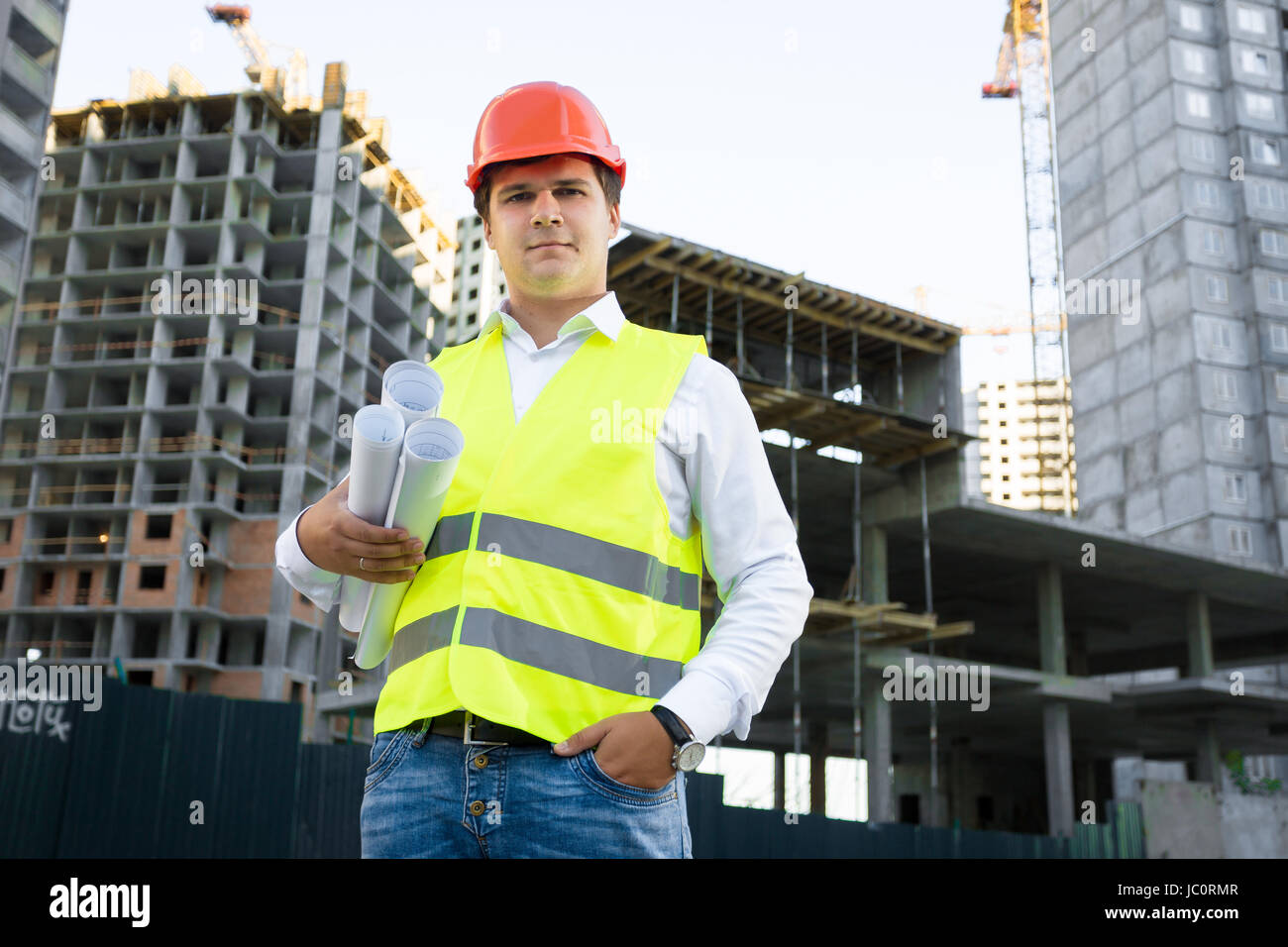 Portrait of site manager posing with blueprints against unfinished ...