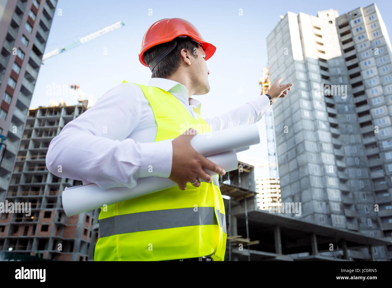 Closeup portrait of foreman with blueprints pointing hand at high ...