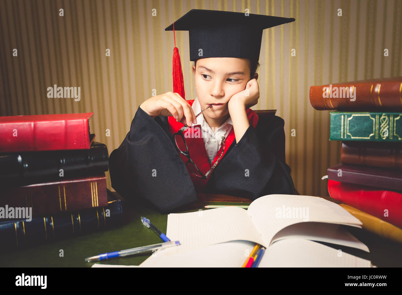 Toned portrait of thoughtful smart girl in graduation hat and gown at ...