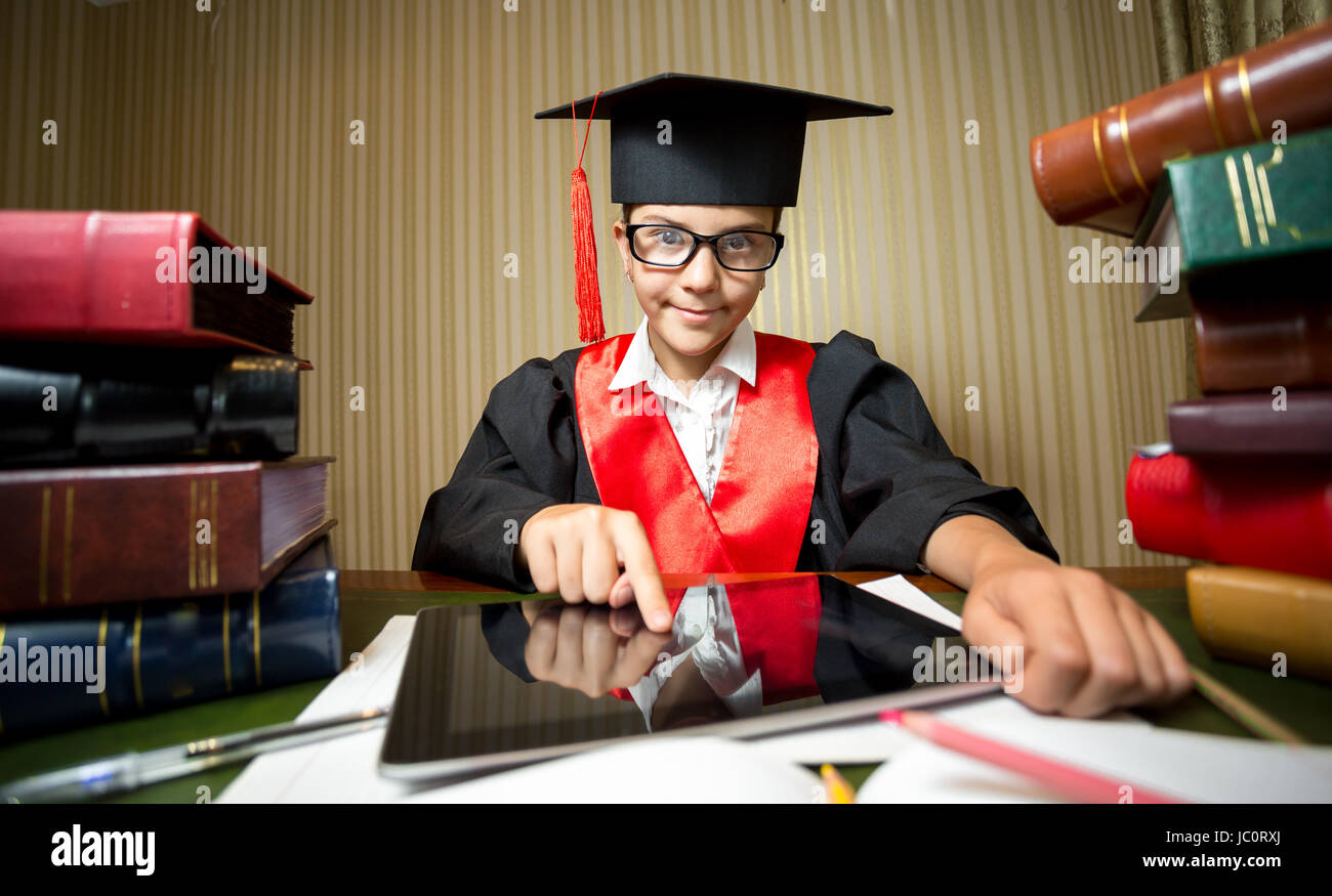 Portrait of smart girl in graduation cap using digital tablet at ...