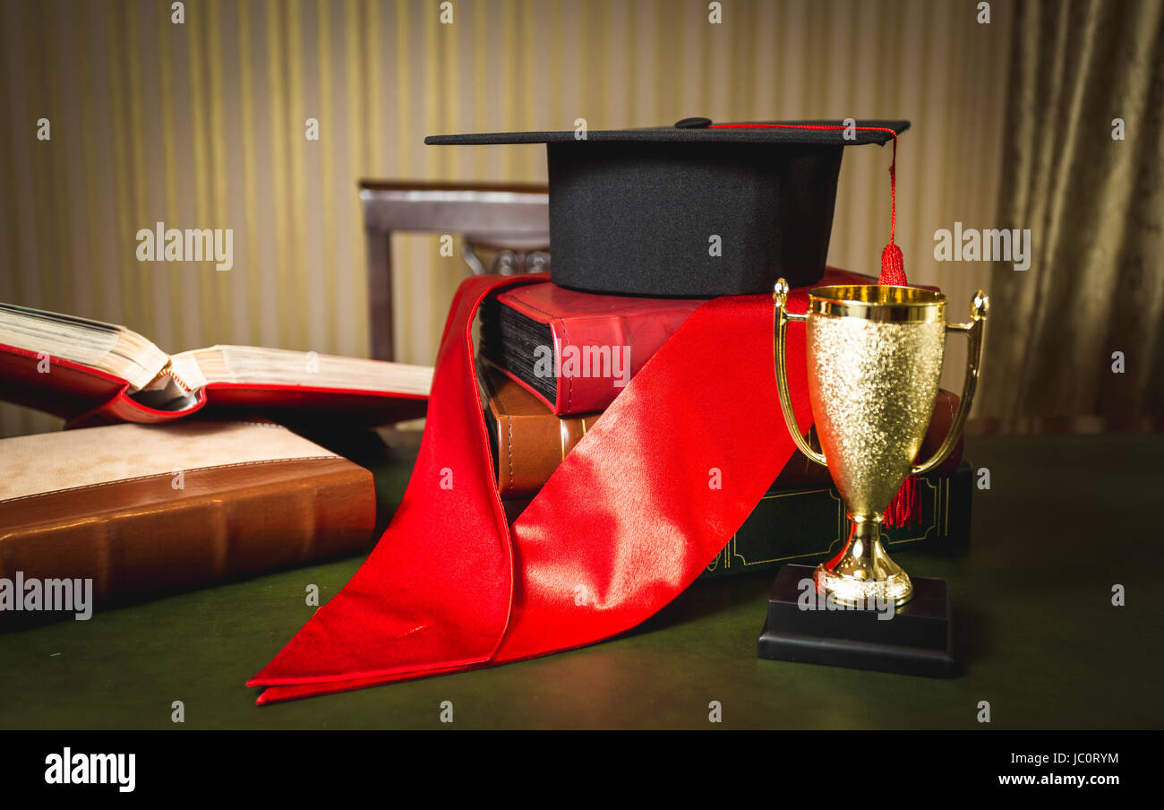 Closeup photo of graduation hat, red ribbon and golden cup for first ...