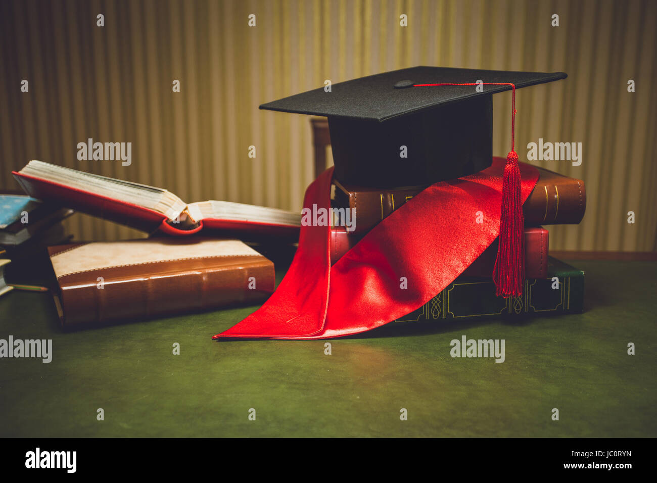 Toned closeup photo of red ribbon and graduation cap on classic table ...