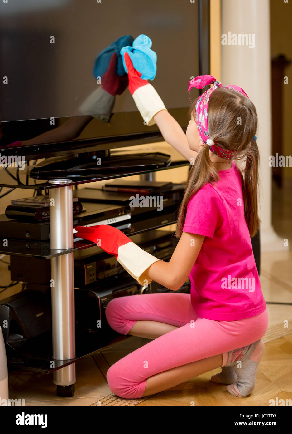 Little girl in rubber gloves cleaning TV screen from dust with blue ...